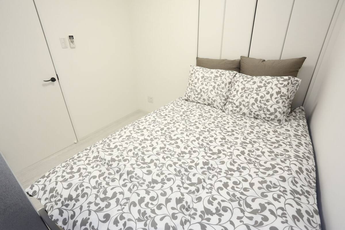 Um quarto com uma cama, duas almofadas, uma porta e um interruptor de luz.