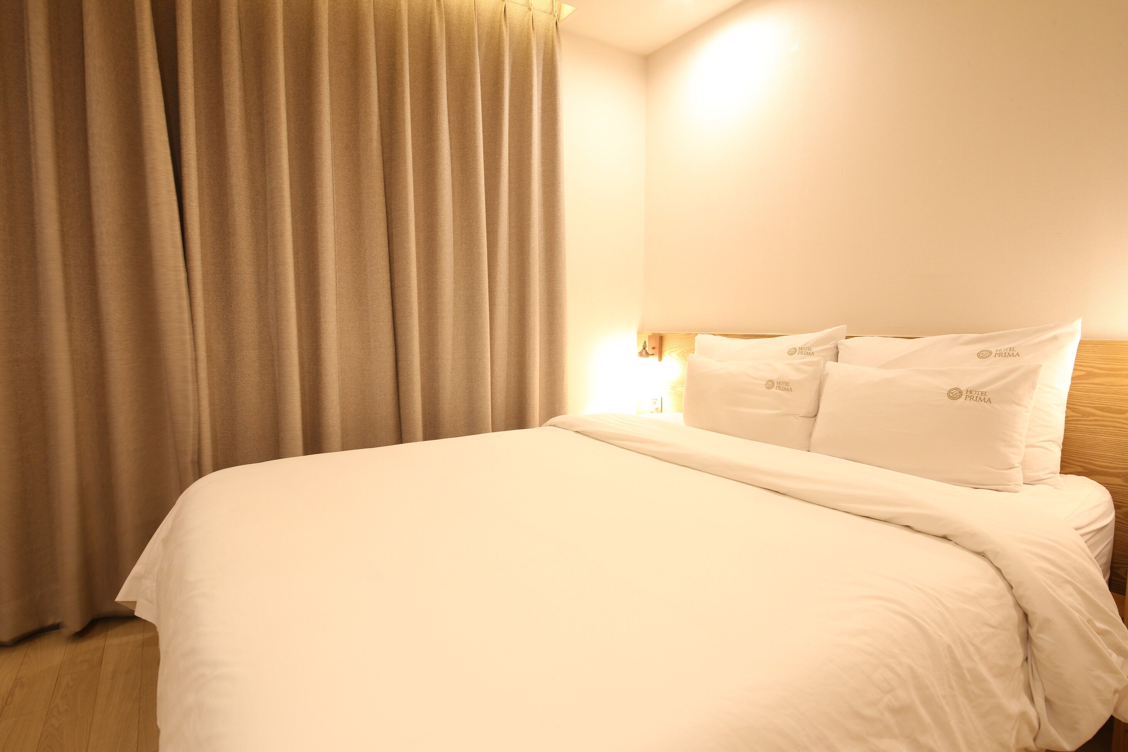 Uma cama bem arrumada com roupa de cama e almofadas brancas, cabeceira de madeira e uma luminária na parede.
