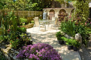 Um pátio com mesa e cadeiras, rodeado por vasos de plantas e flores.