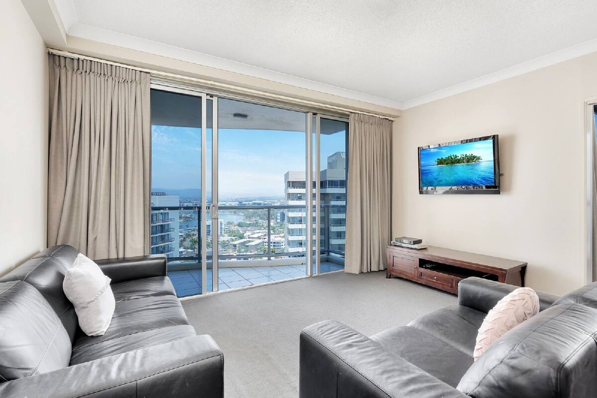 Uma sala de estar moderna com uma grande porta de vidro deslizante que dá para uma varanda com vista para a cidade.
