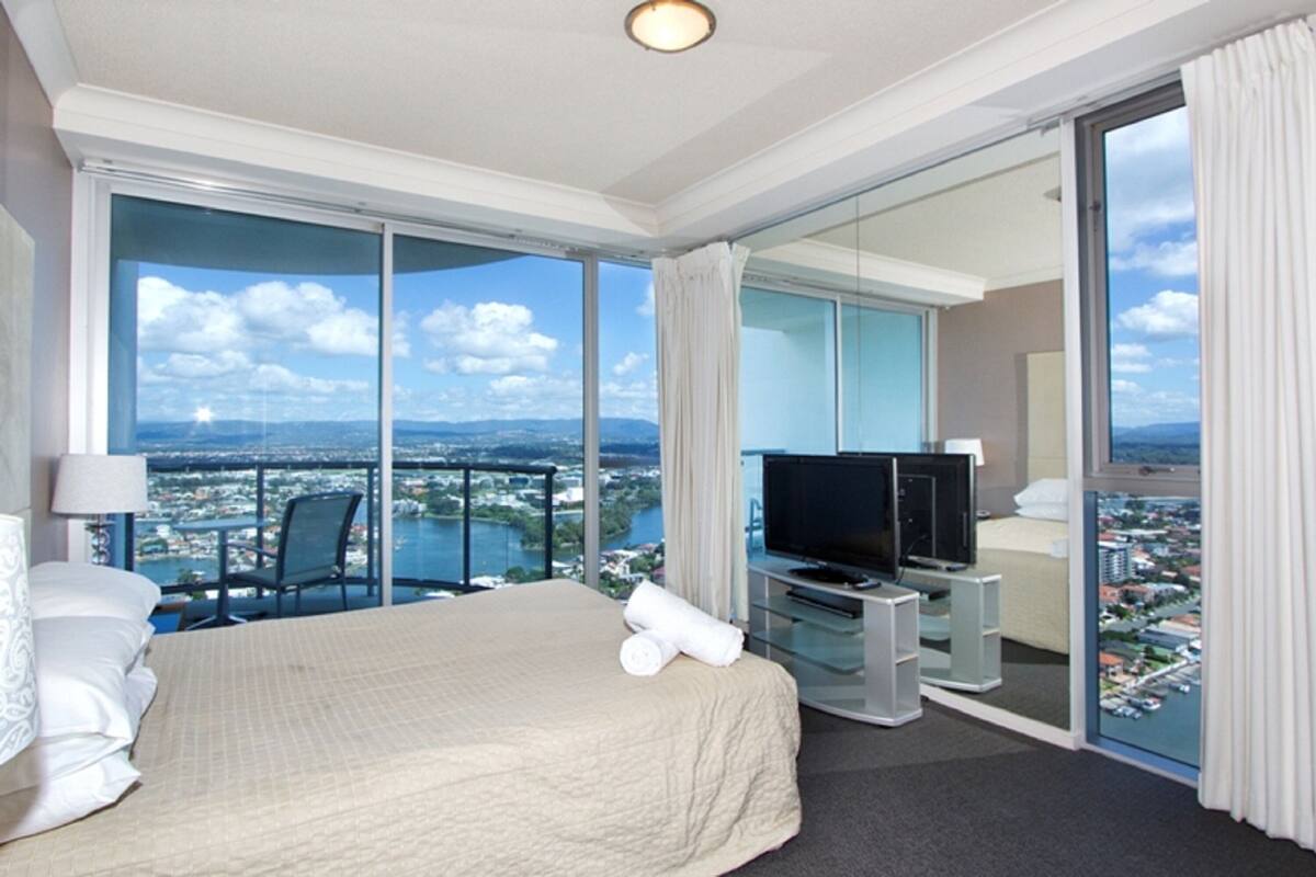Quarto de hotel com uma cama grande, televisão e varanda com vista para a cidade.