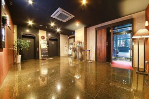 Um saguão de hotel com piso de azulejos polidos, um elevador, um café e uma mesa de recepção.