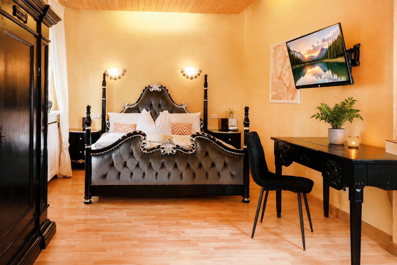 Quarto com uma cama grande, mesas de cabeceira, uma escrivaninha e uma cadeira.