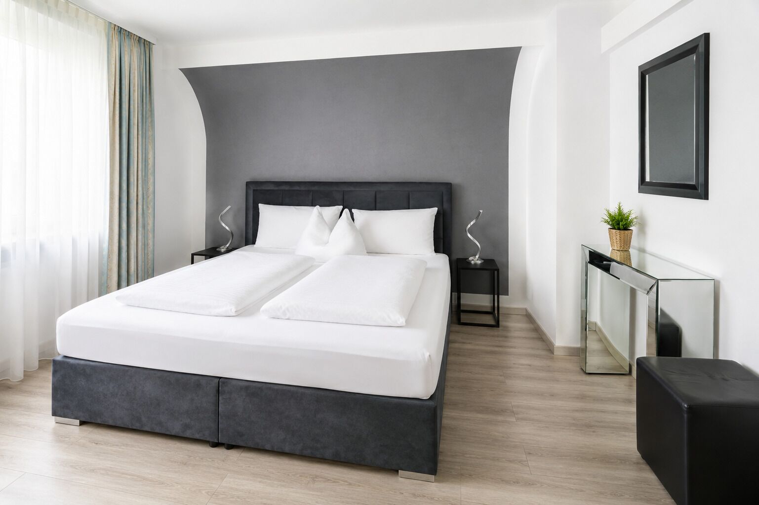 Quarto de hotel moderno com uma cama grande, mesas de cabeceira, um aparador e um vaso de planta.