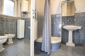 Casa de banho com duas casas de banho, um bidé, chuveiro com cortina e um lavatório.