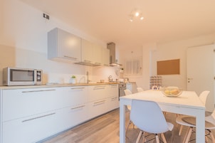 Uma cozinha moderna com armários brancos, um micro-ondas e uma mesa de jantar com cadeiras.