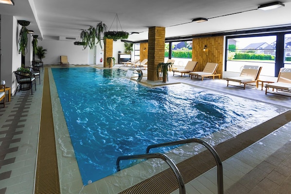 Piscina interna com espreguiçadeiras e vista para o exterior.