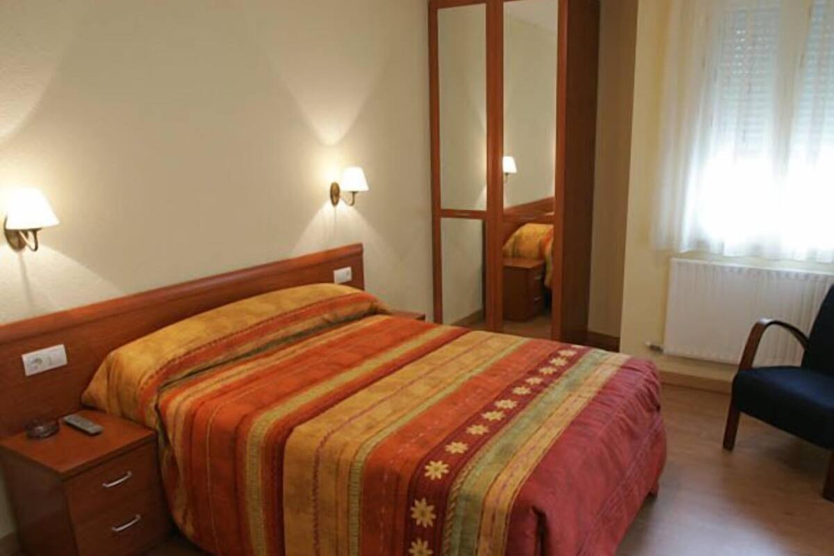 Quarto com cama, mesa de cabeceira e espelho.