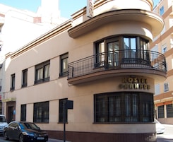 Um edifício com fachada curva, uma placa com a inscrição "Hostal Granada" e um carro preto estacionado em frente.