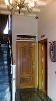 Uma porta de madeira imponente com detalhes decorativos na parte superior, uma escadaria com degraus escuros e uma televisão fixada na parede.