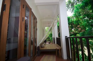 Uma varanda com um banco de madeira e um tapete tecido, cercada por vegetação exuberante.
