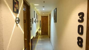 Corredor de hotel com uma porta de madeira no final, número 308 na parede, e uma placa de loja à esquerda.