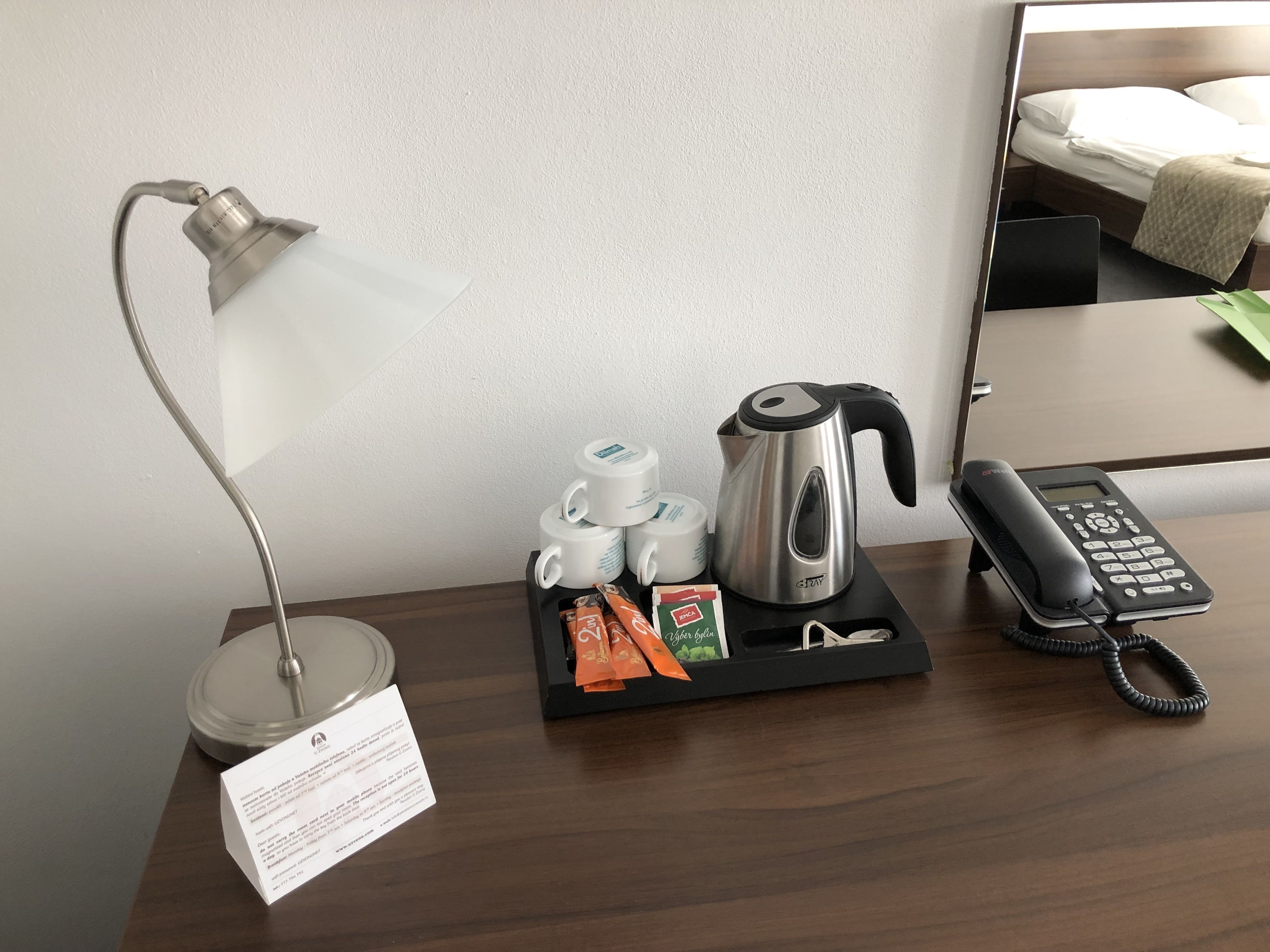 Mesa de hotel com luminária, cafeteira, telefone e bandeja com chávenas de café e petiscos.