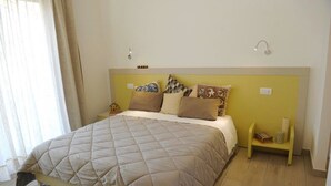 Quarto com cama, almofadas, mesas de cabeceira e janela com cortinas.