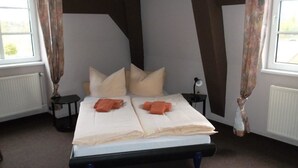 Quarto com cama, almofadas, mesa de cabeceira, luminária e cortinas.