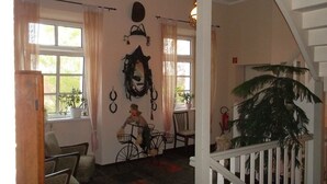 Quarto com cadeira de madeira, mesa pequena, espelho decorativo e escultura de bicicleta.