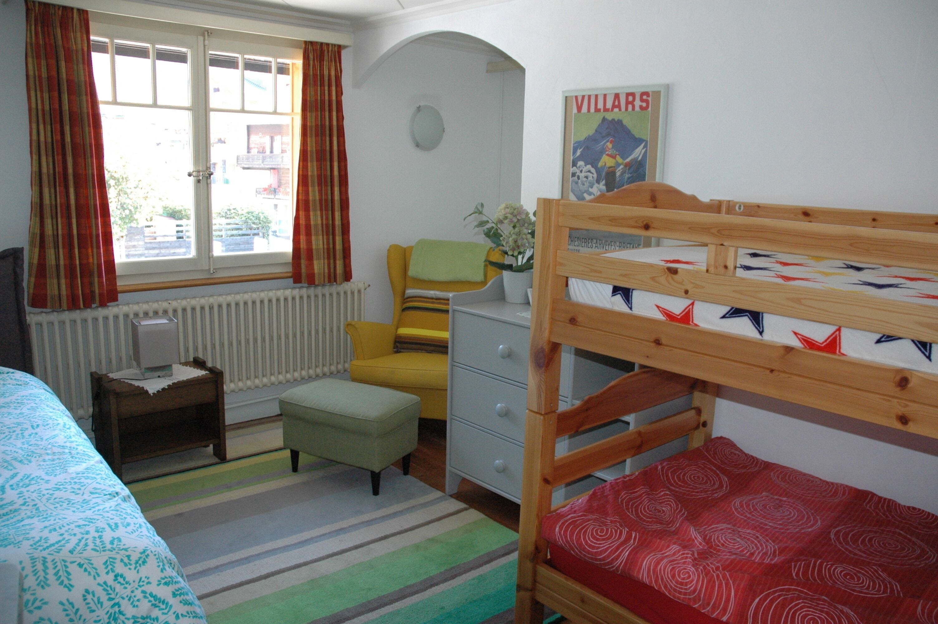Quarto com cama beliche, uma cadeira, escrivaninha e radiador.
