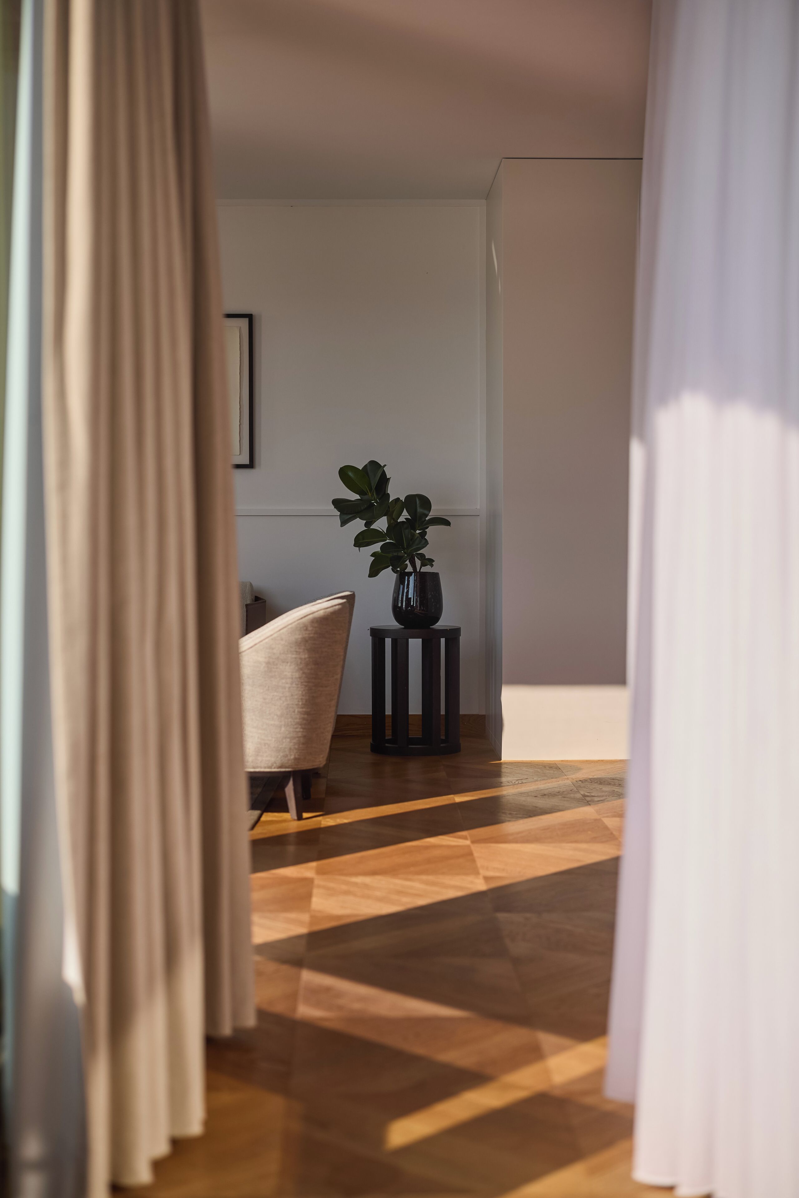Um corredor com soalho de madeira estampado, uma cadeira, uma pequena mesa com uma planta e um quadro na parede.