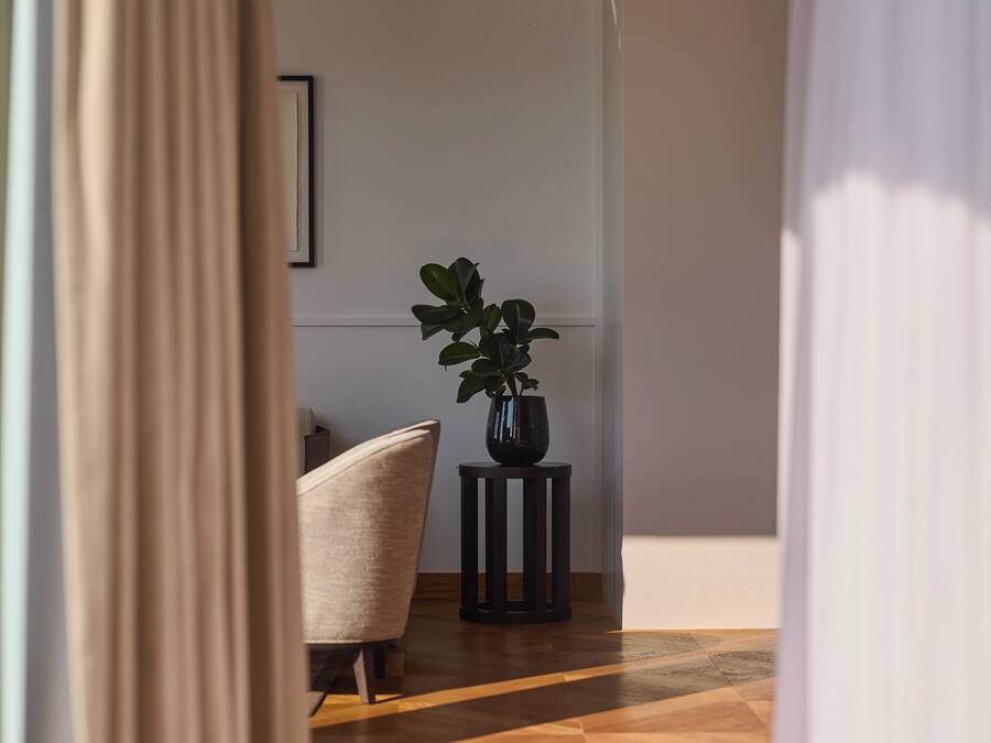 Um corredor com soalho de madeira estampado, uma cadeira, uma pequena mesa com uma planta e um quadro na parede.