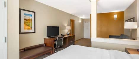 Quarto de hotel com cama, escrivaninha, cadeira, televisão e um quadro na parede.