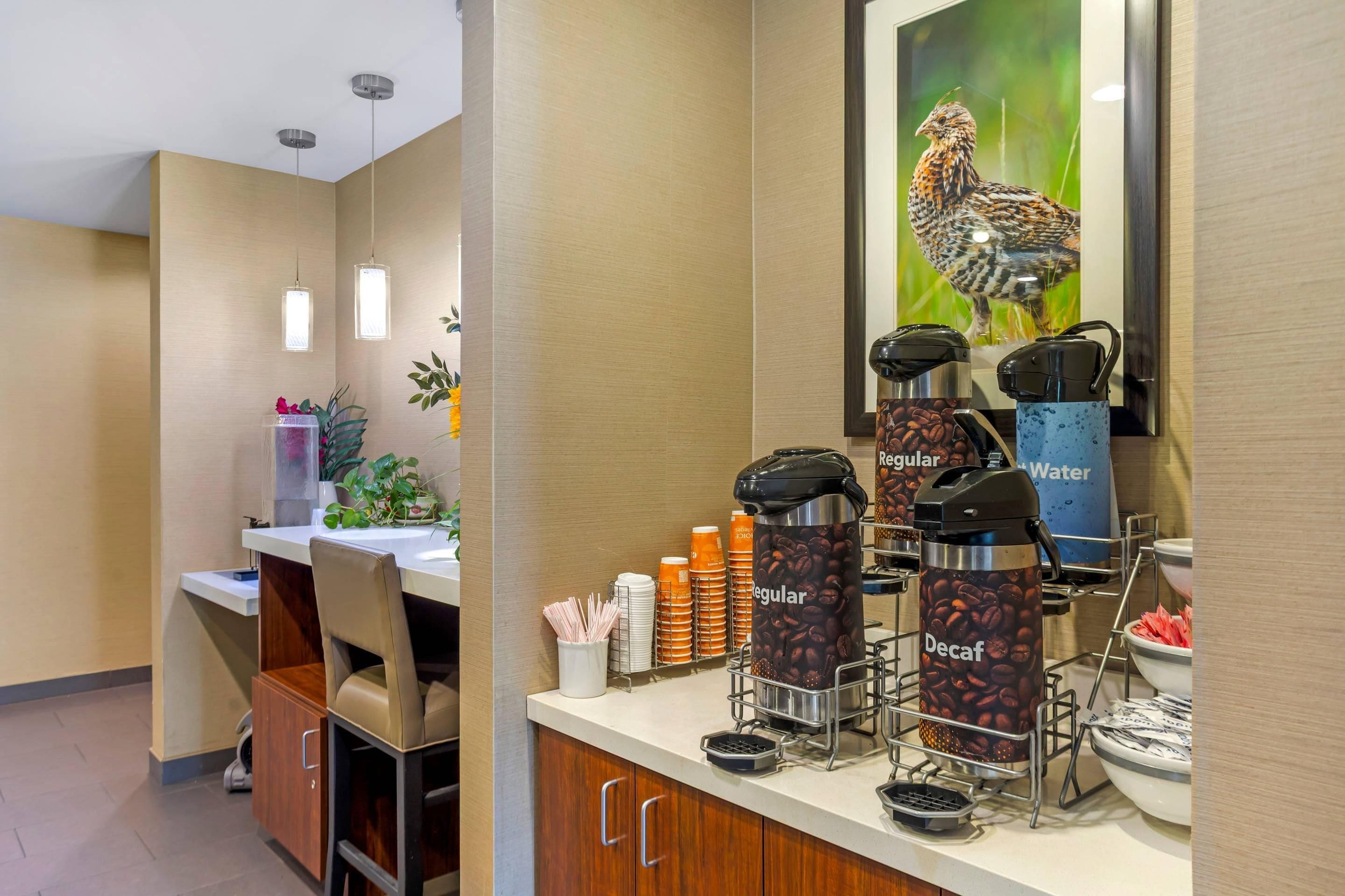 Quarto de hotel com cozinha compacta, espaço para café e um quadro de um pássaro na parede.