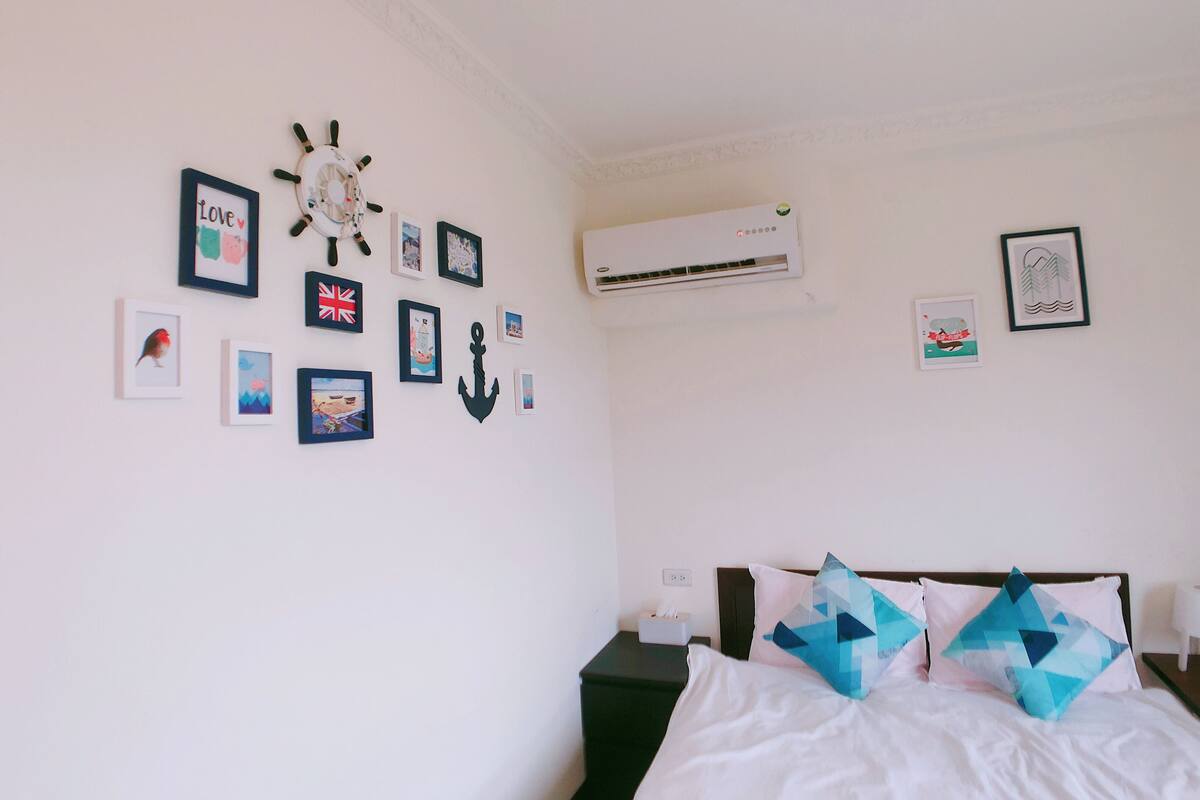 Quarto de hotel com cama, mesa de cabeceira e parede decorada com diversas molduras.