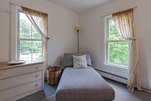 Um quarto com uma cama, cômoda, abajur e janela com cortinas.