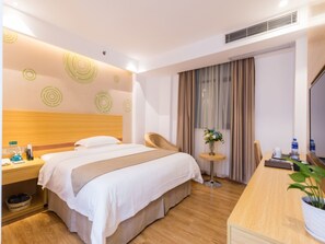 Quarto de hotel com cama, mesa de cabeceira, cadeira, escrivaninha e uma pequena mesa com um vaso de flores.