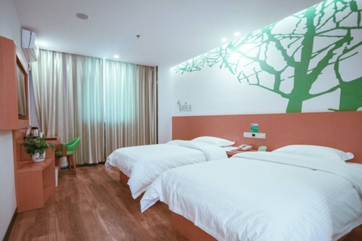Quarto de hotel com duas camas, piso de madeira, uma cadeira verde, uma planta em vaso e um mural na parede.