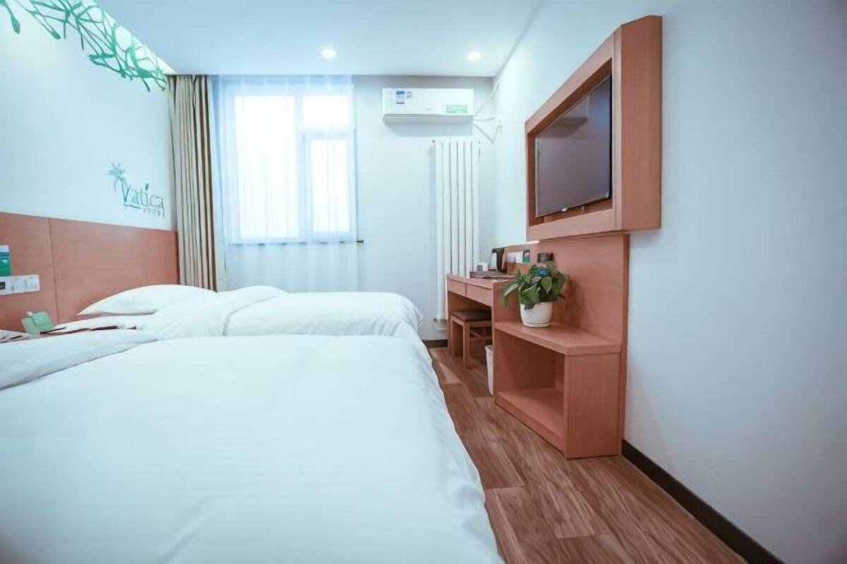 Quarto de hotel com duas camas, uma escrivaninha, um espelho e um vaso de plantas.