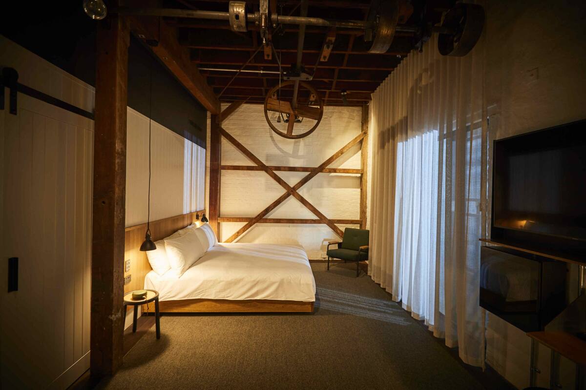 Quarto com teto de madeira, cama, televisão e uma cadeira.