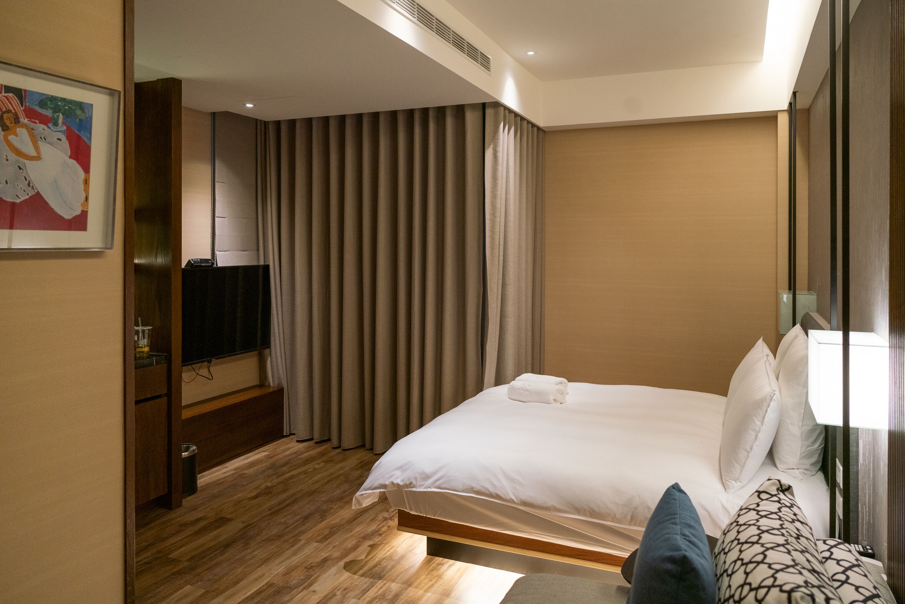 Quarto de hotel com uma cama grande, televisão, piso de madeira e um quadro na parede.