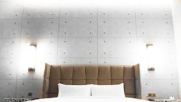 Quarto de hotel moderno com uma cama grande, cabeceira estofada e parede texturizada com iluminação embutida.
