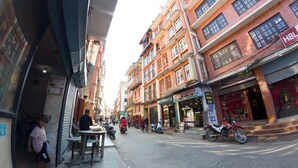 Uma rua estreita ladeada por edifícios altos, alguns com estabelecimentos comerciais no andar térreo.