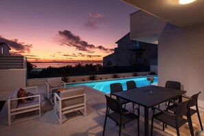 Um terraço no telhado com piscina, área de estar externa e vista para o pôr do sol.