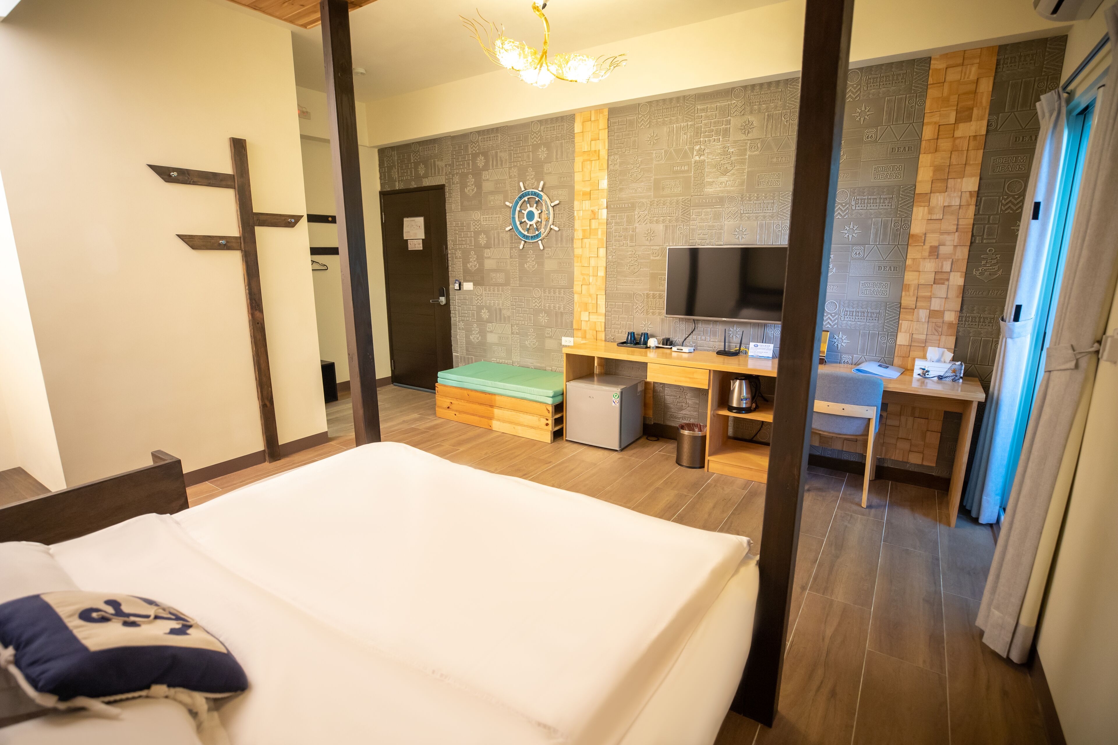 Quarto de hotel moderno com cama, escrivaninha, televisão e uma pequena cozinha equipada.