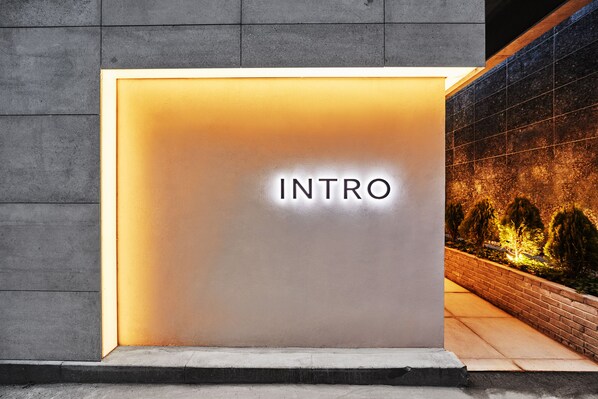 Uma entrada moderna com estrutura metálica e a palavra "INTRO" iluminada na parede.