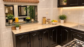 Cozinha com armários escuros, bancada de mármore, fogão a gás e diversos utensílios de cozinha, como uma tigela de frutas e uma garrafa de suco.