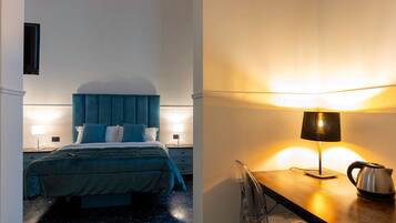 Quarto de hotel com cama, abajures, escrivaninha com luminária e chaleira.