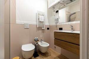Casa de banho moderna com sanita, bidé, toucador com espelho e suporte para toalhas.