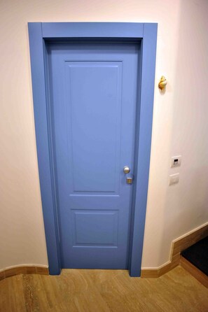 Uma porta azul com puxador prateado, um pequeno objeto decorativo na parede e um interruptor de luz.