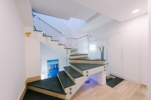 Escadaria moderna com guarda-corpos de vidro e vista para o mar através de uma porta de vidro.