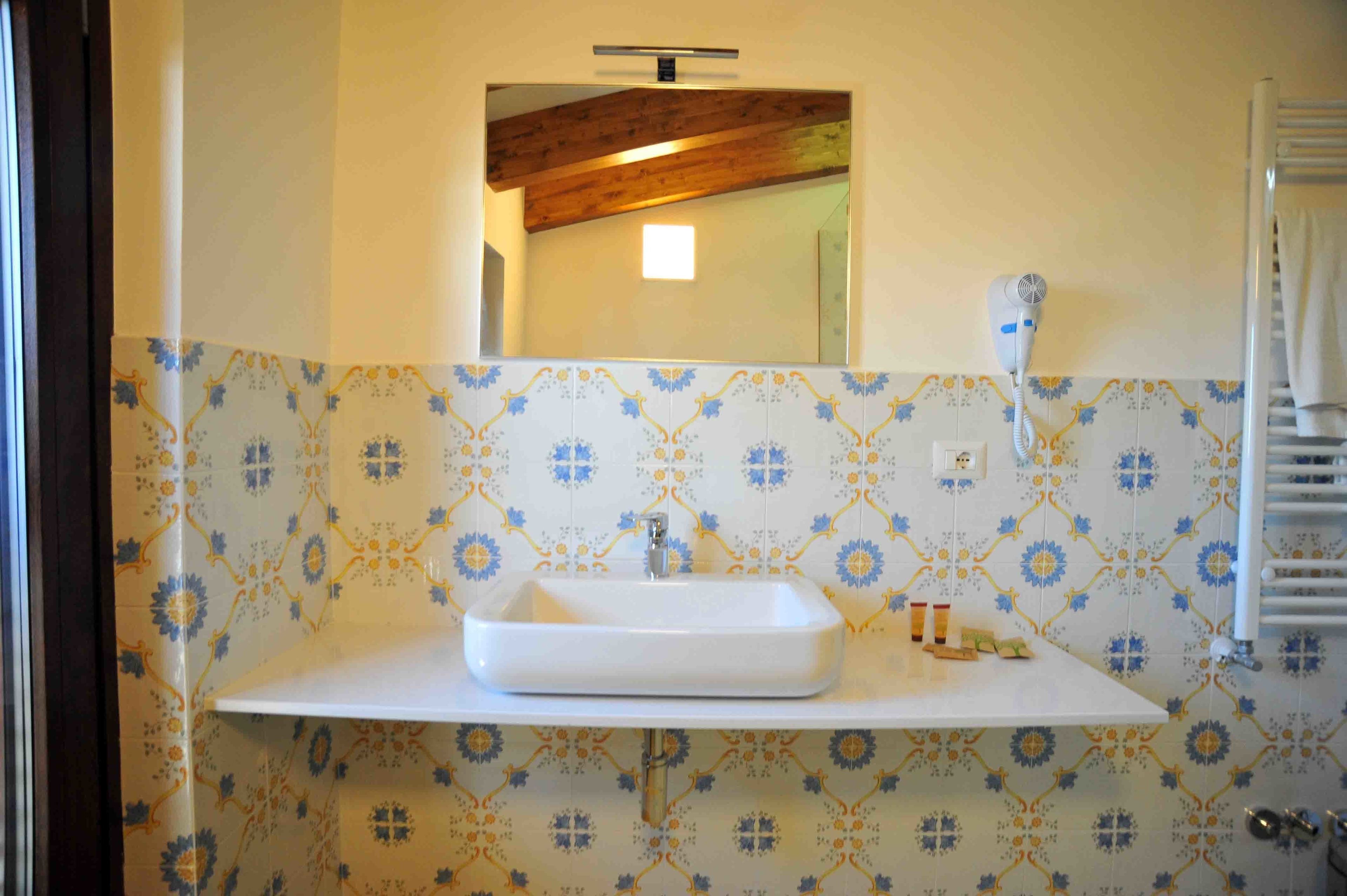 Casa de banho com lavatório branco, espelho em cima e barra de toalhas à direita.