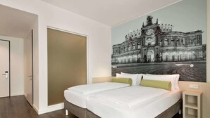 Uma cama de casal com roupa de cama branca, uma cabeceira e uma mesa de cabeceira com uma luminária.