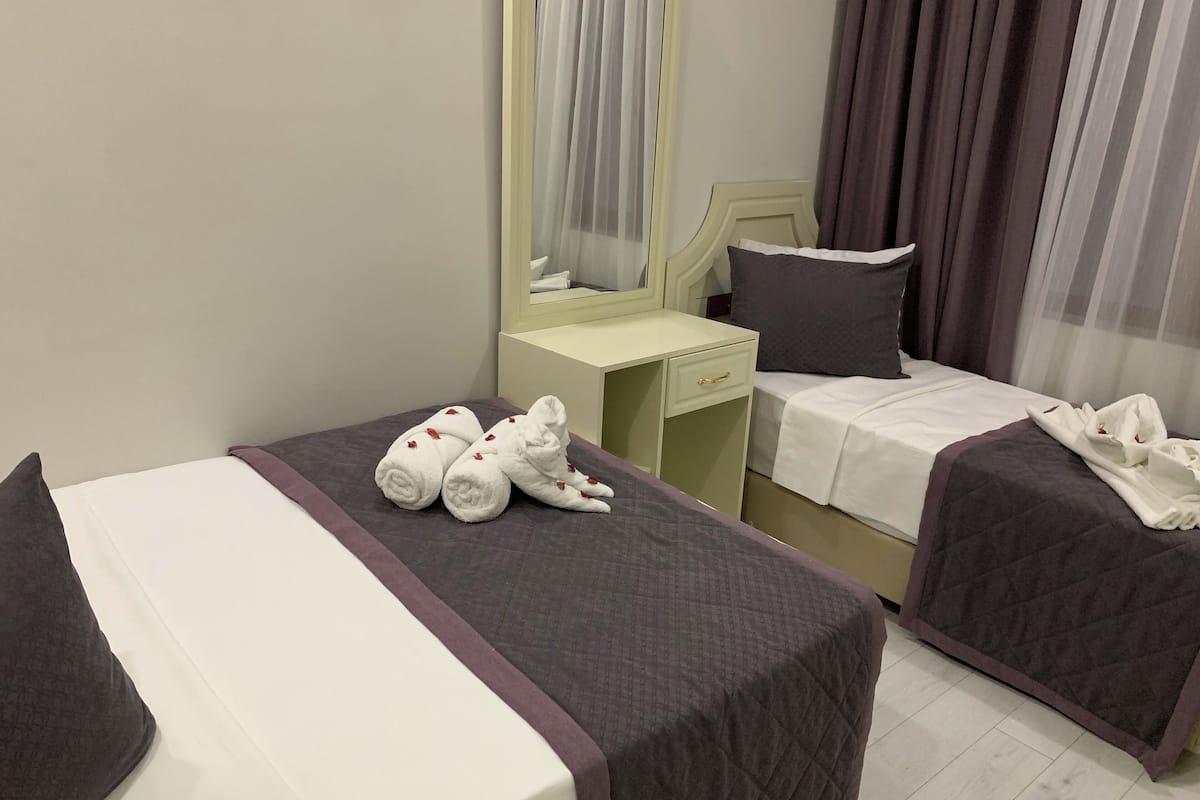Quarto de hotel com duas camas, uma secretária pequena, um espelho e uma janela com cortinas.