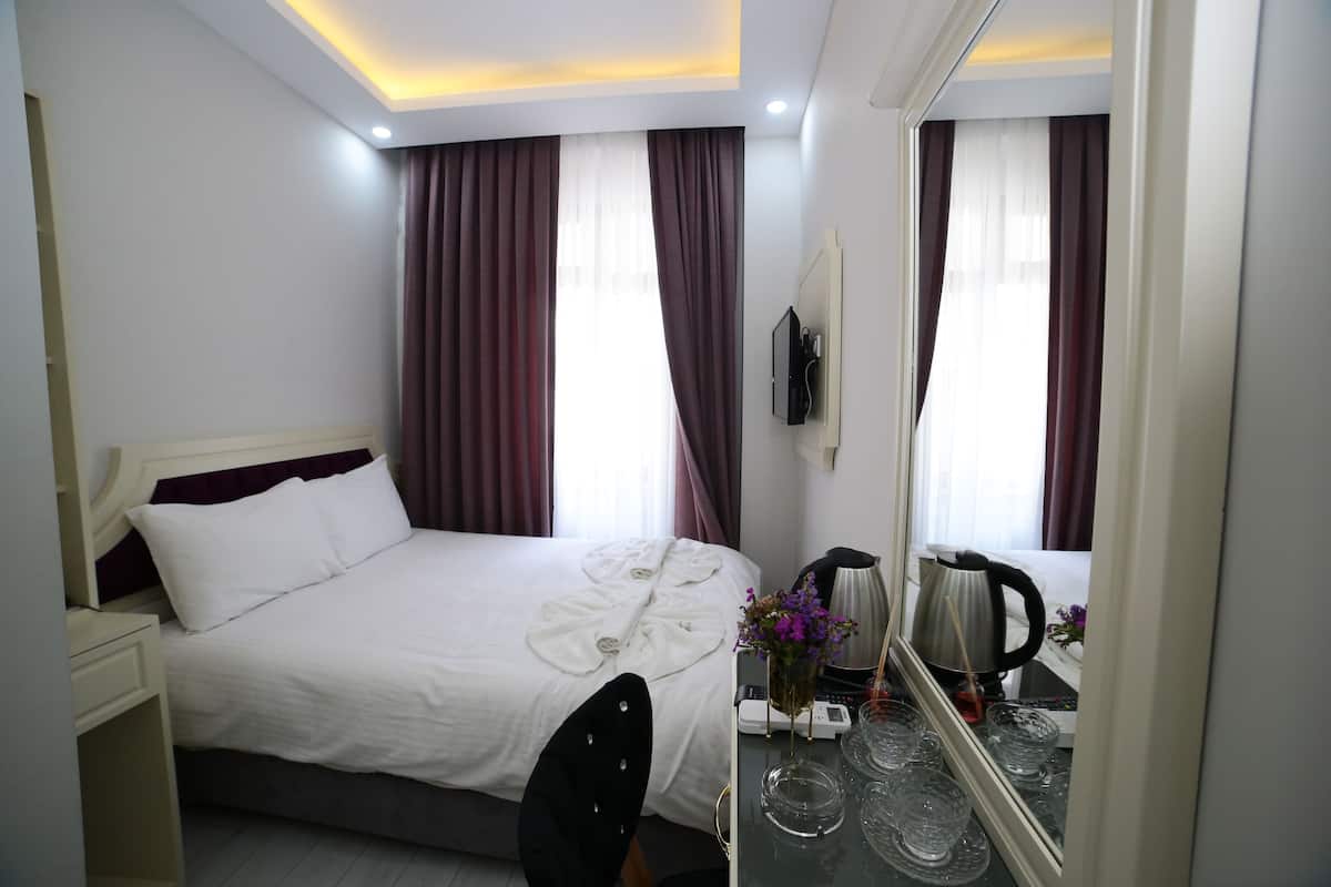 Quarto de hotel com uma cama, mesa de cabeceira, espelho e janela com cortinas.