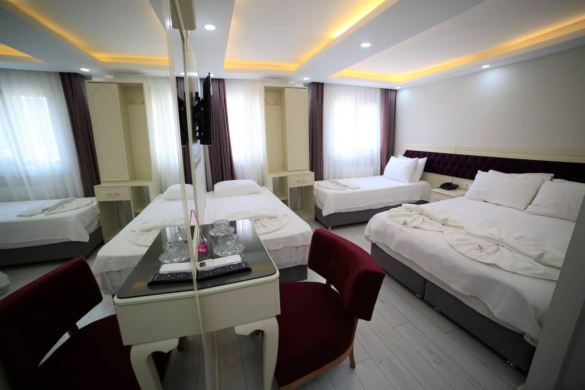 Quarto de hotel com duas camas, uma escrivaninha e uma cadeira. Há cortinas, um guarda-roupa e uma televisão.