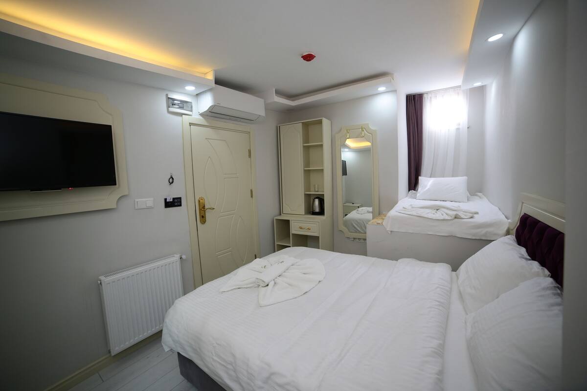 Quarto de hotel com uma cama grande, televisão na parede, espelho, guarda-roupa e radiador.
