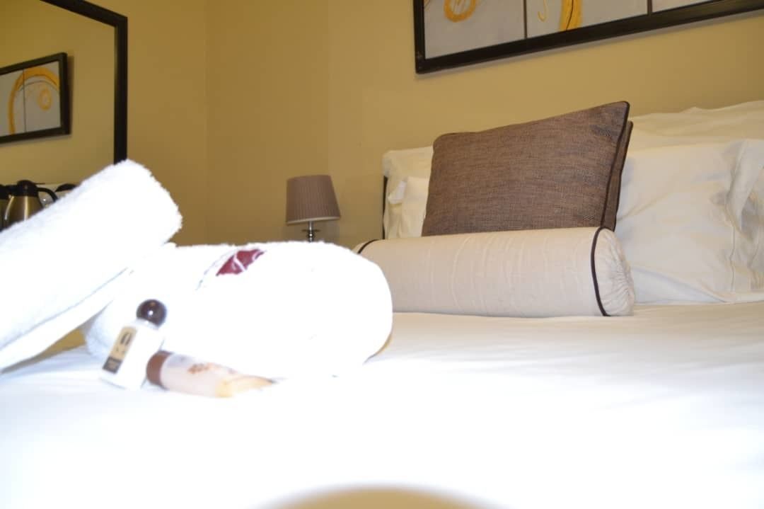 Quarto de hotel com cama, almofadas, luminária e uma obra de arte na parede.