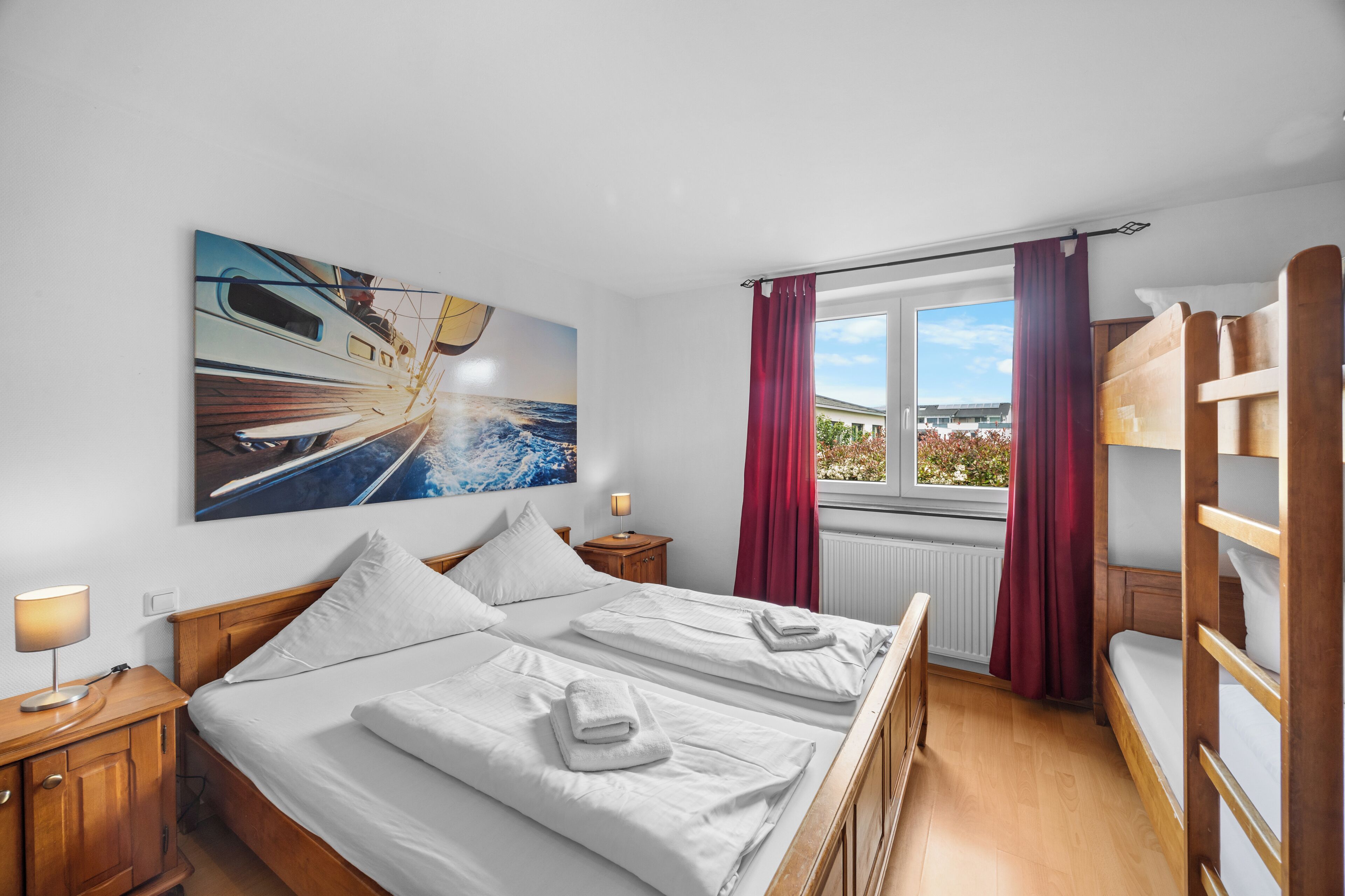 Quarto de hotel com cama, janela com cortinas, cabeceira de madeira, mesa de cabeceira e um quadro pendurado na parede.